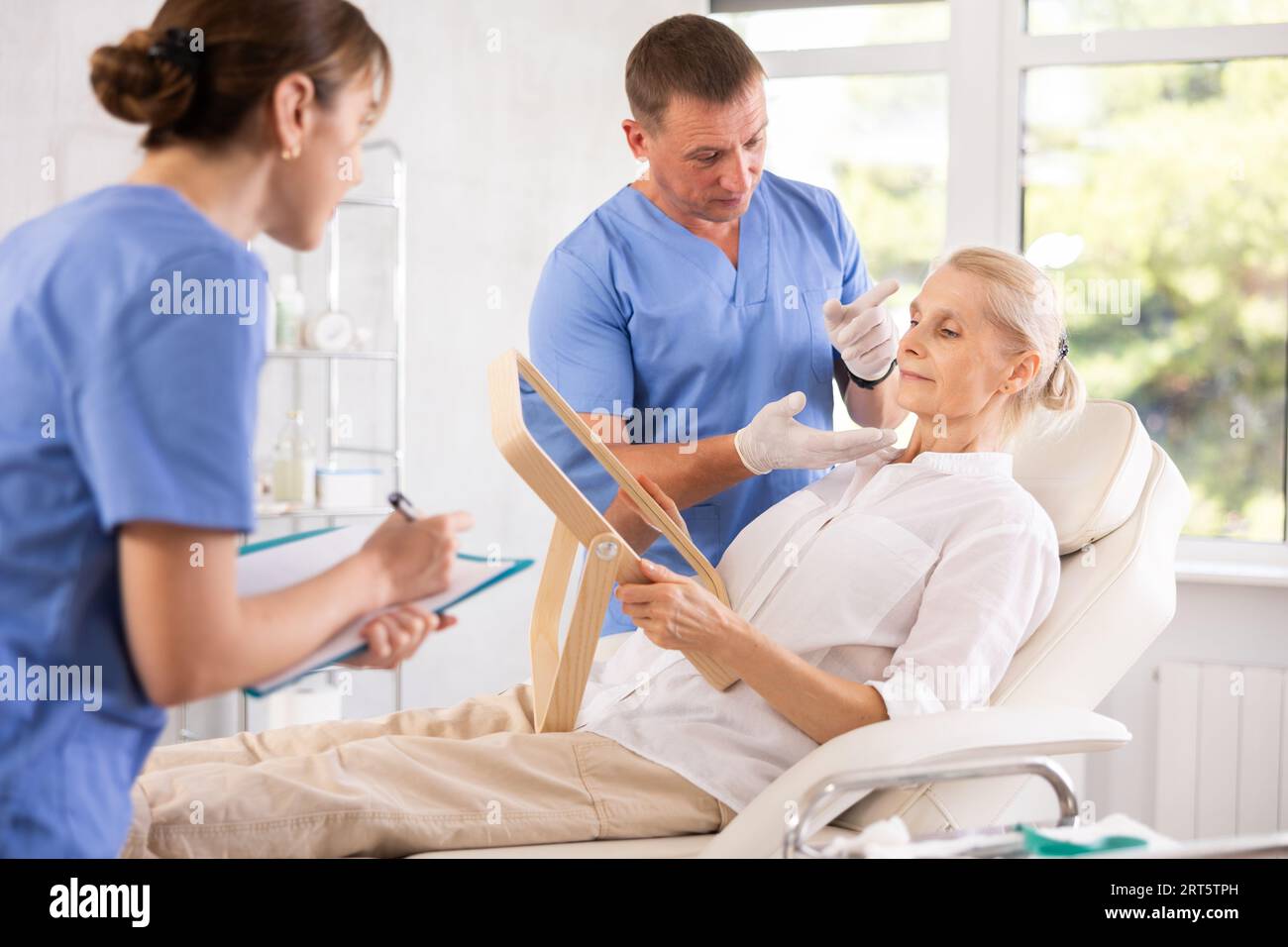 Man dermatologist examines skin of senior womans face, female nurse ...