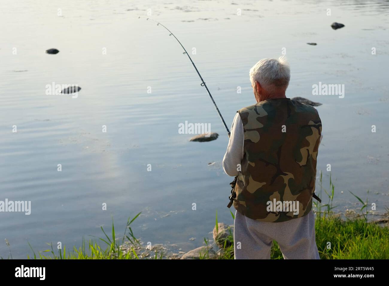 Old man fishing. Senior gray haired fisherman throws a spinning from ...