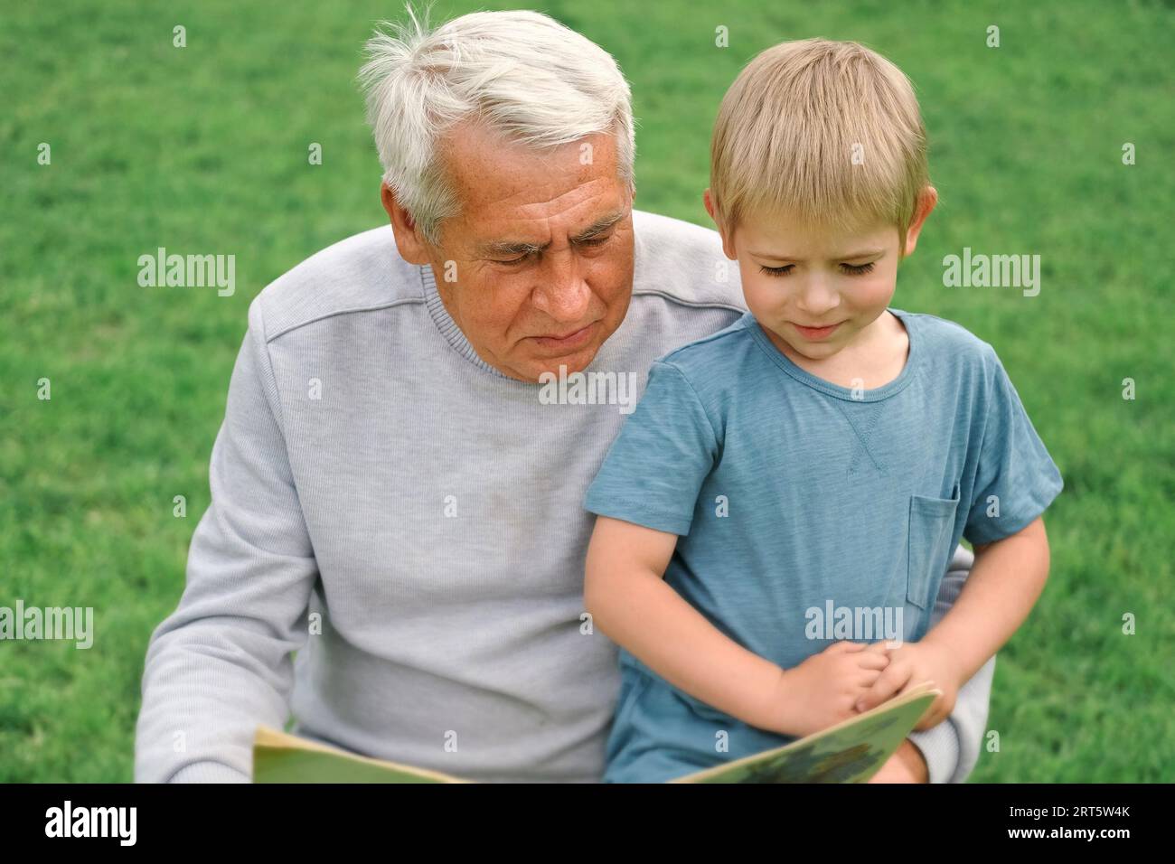 Happy grandfather reading book to curious grandson outdoors. Close up ...