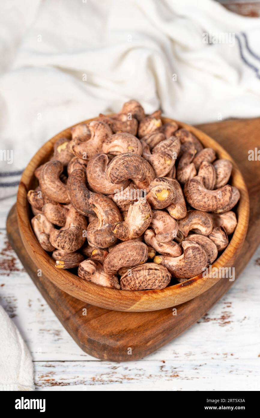 Cashews with shell in wood bowl. Shelled cashew on white wood ...
