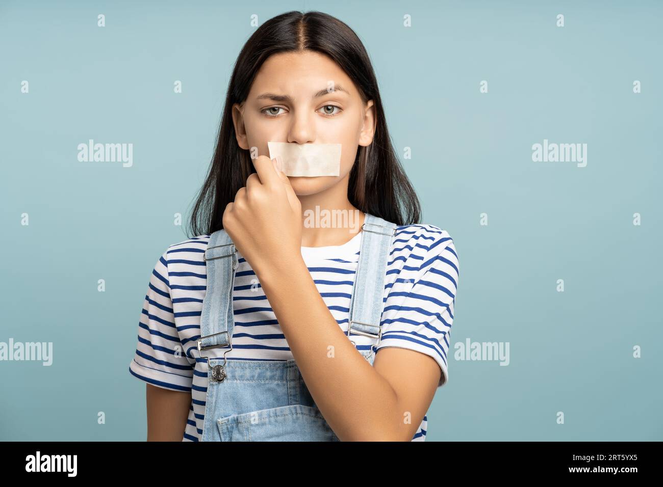 Sad frustrated teen girl rips off tape from mouth on turquoise ...