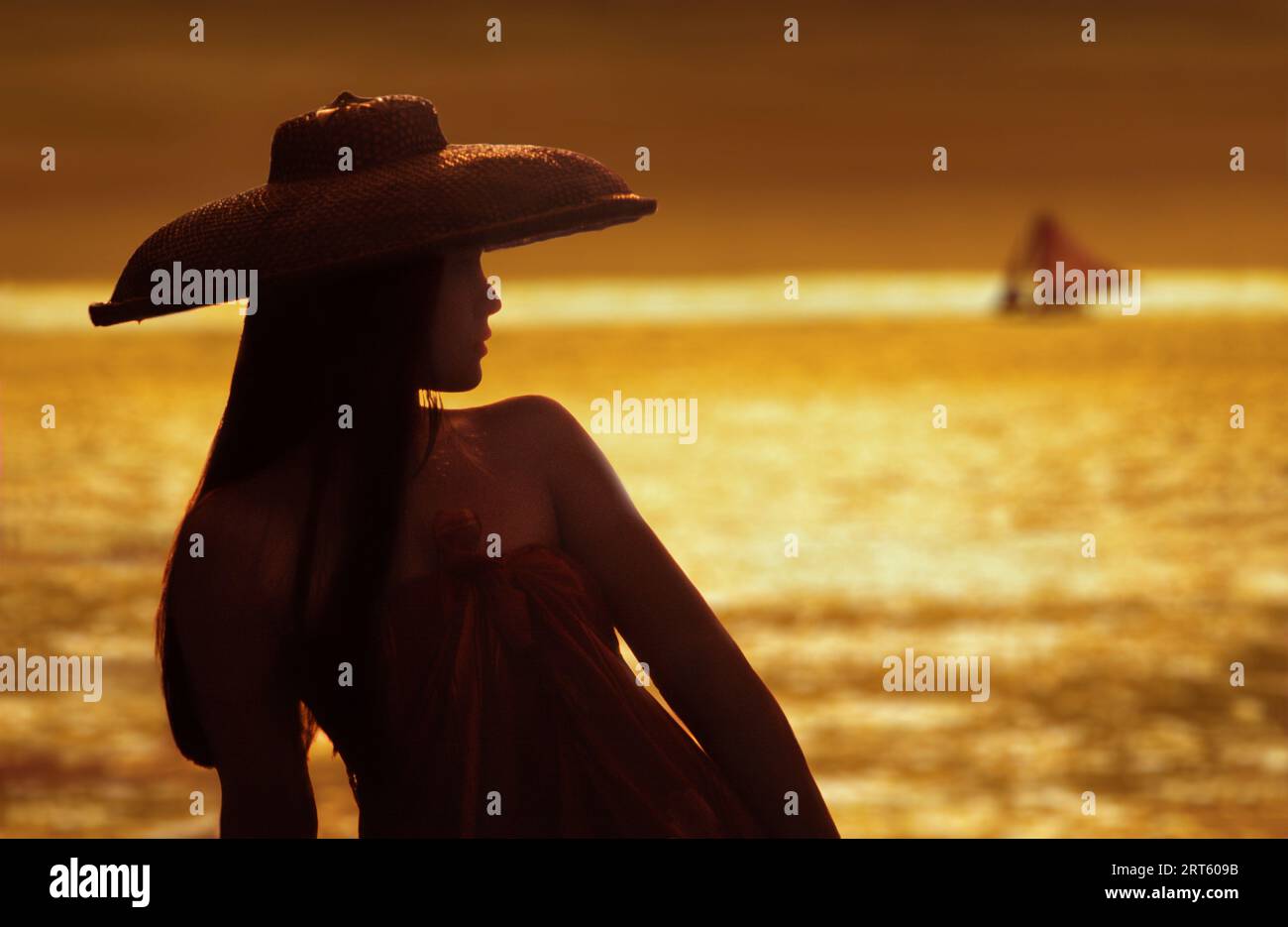 A Filipina wearing a traditional straw hat, in the distance, a sunset ...