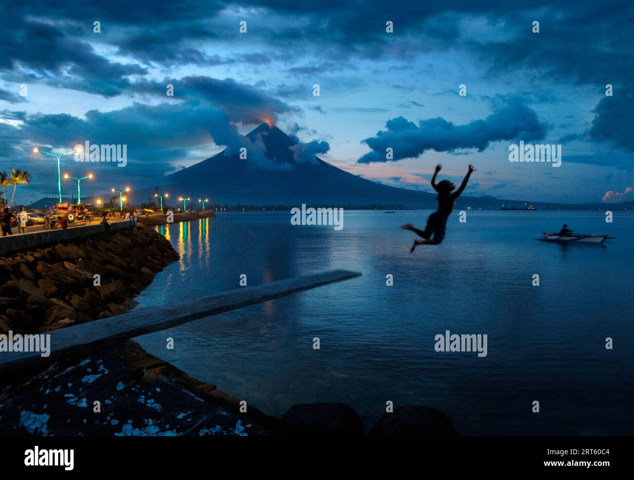 Boy jumping into the sea before a glowing Mayon Volcano Stock Photo - Alamy