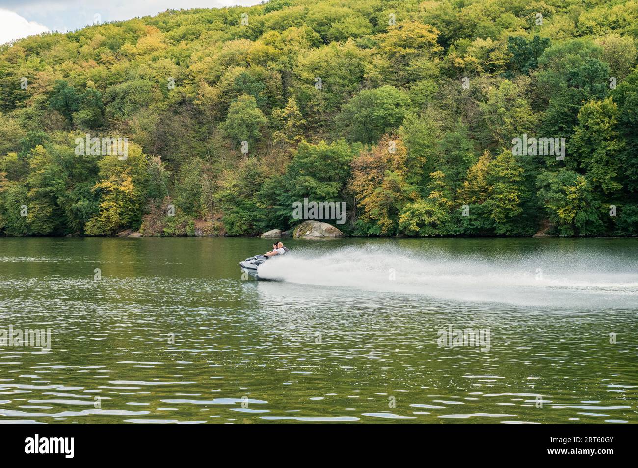 Two people riding jet ski on river with beautiful green trees ...