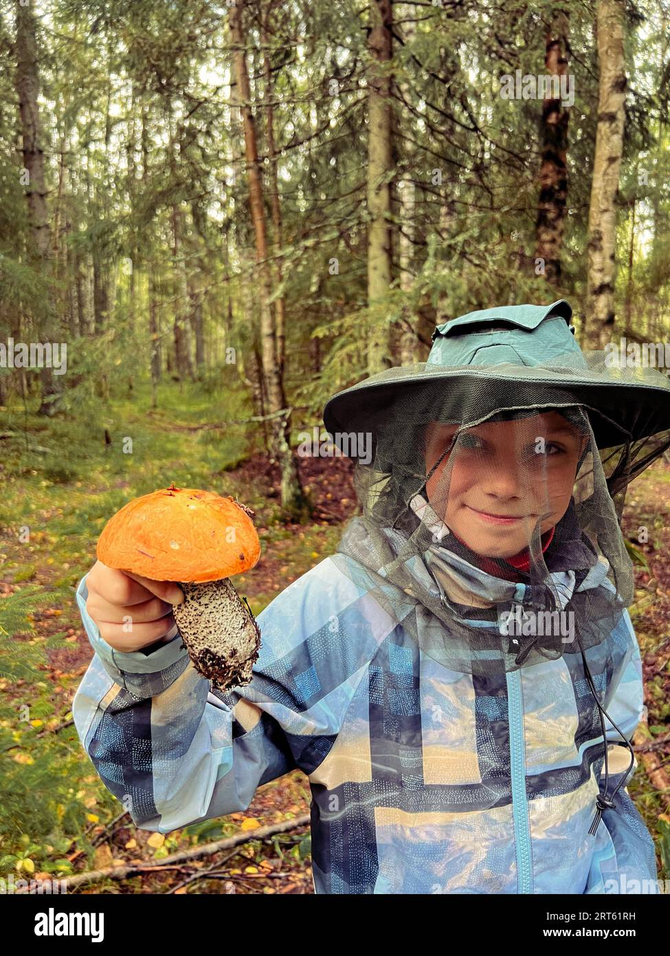 cute caucasian boy wearing anti mosquito hat holding big red boletus ...