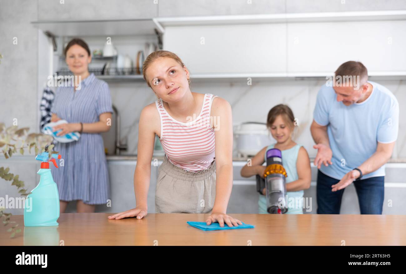 Teenage daughter dusting the table while parents and youngest daughter ...