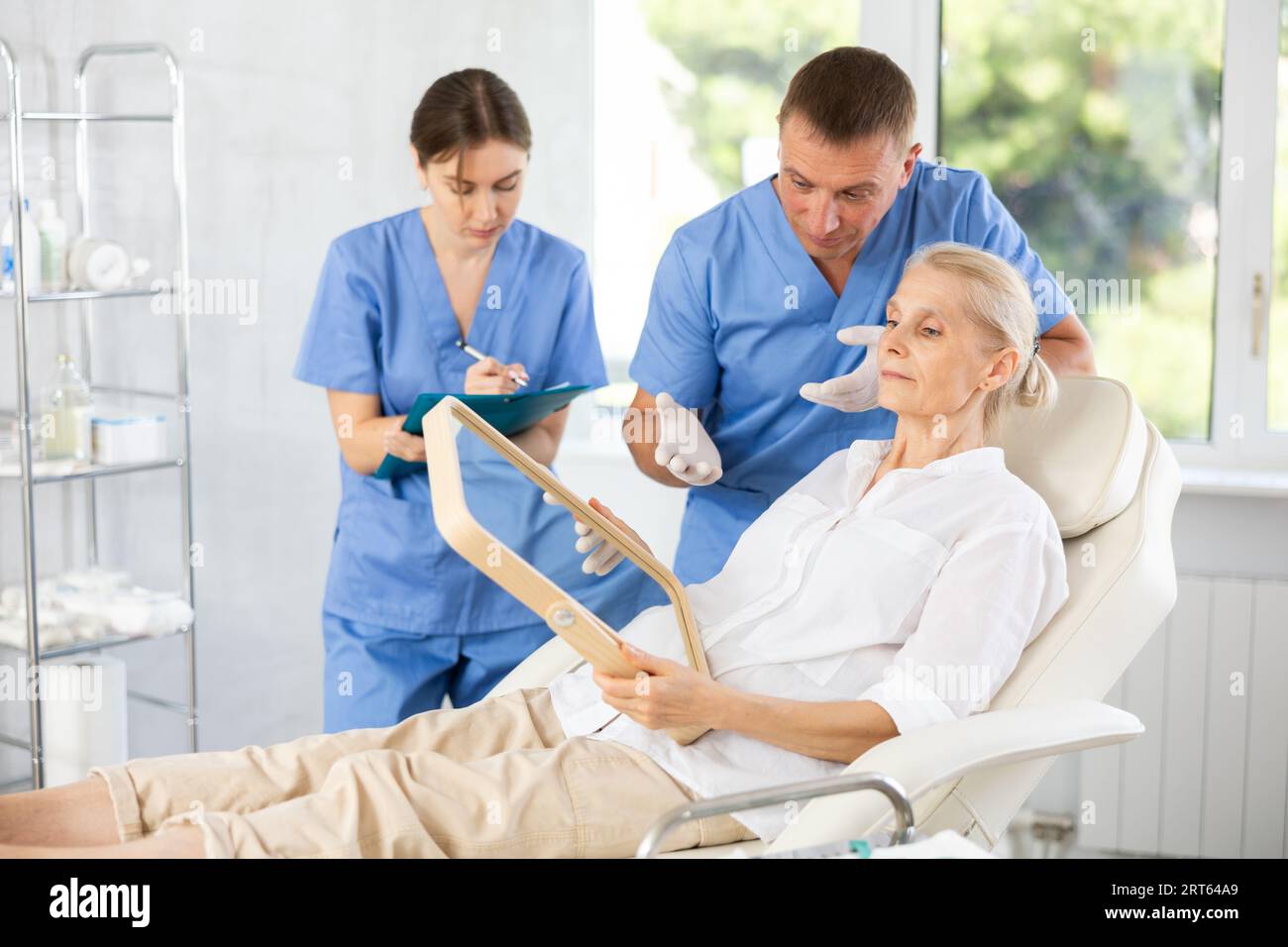 Man dermatologist examines skin of senior womans face, female nurse ...