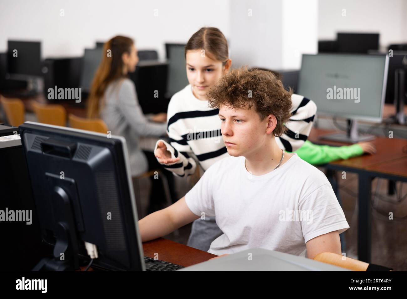 Boy using computer to help girl to solve problem in classroom Stock ...