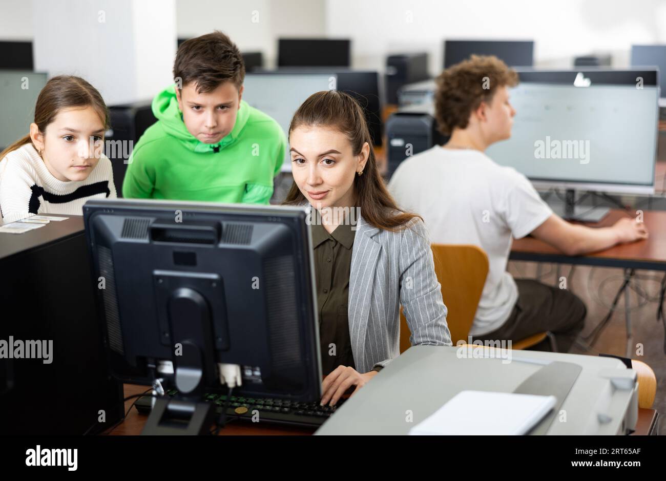 Teacher helping girl and boy to solve computer problem Stock Photo - Alamy