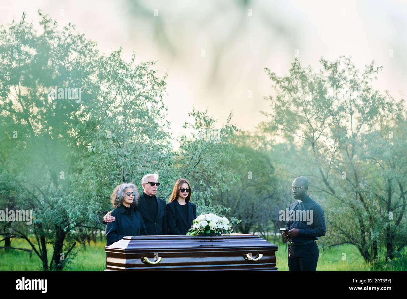 Long shot of mourning family of three and priest in black attire ...