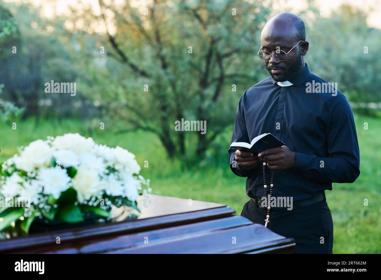 African American pastor with open Holy Bible carrying out funeral ...