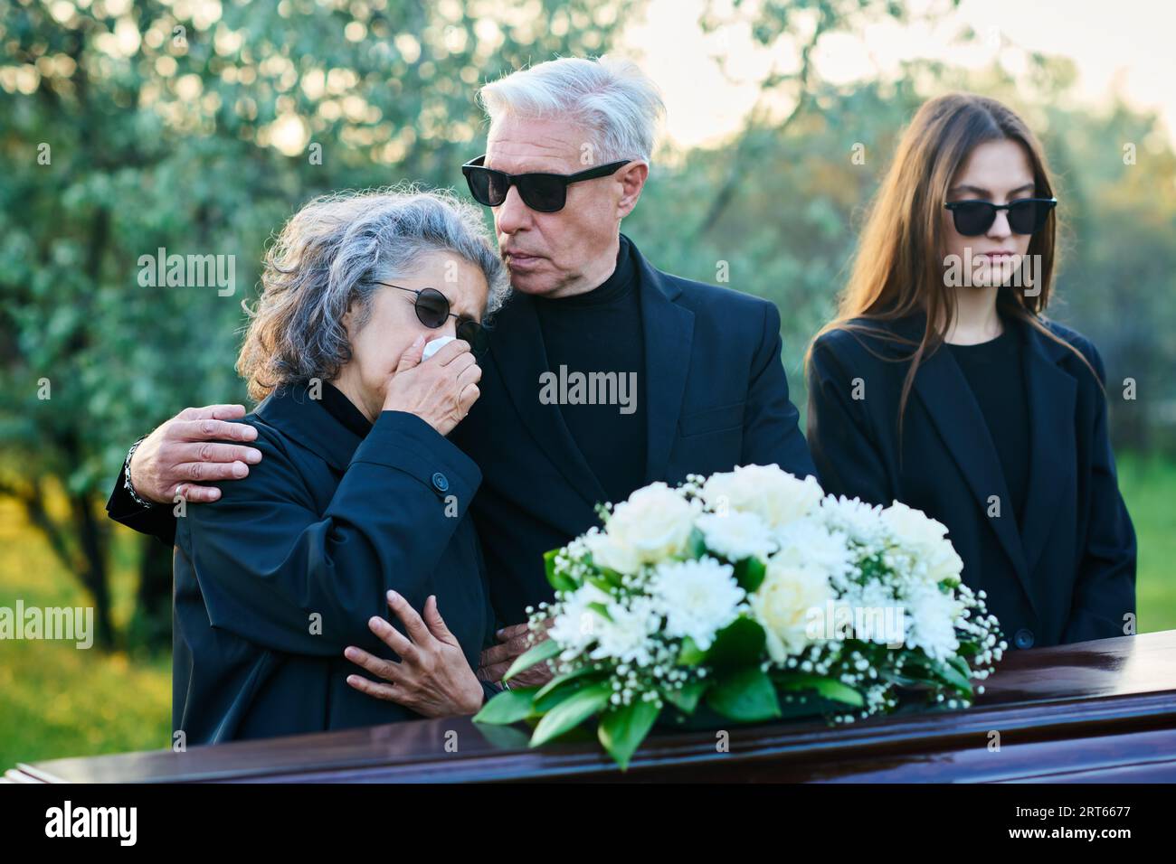 Mature man in black attire and sunglasses consoling his wife lamenting ...