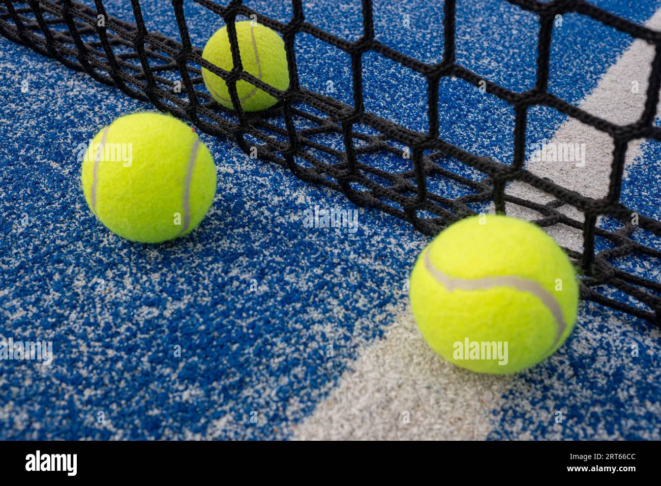 Three yellow balls on floor in front and behind of paddle net in blue ...