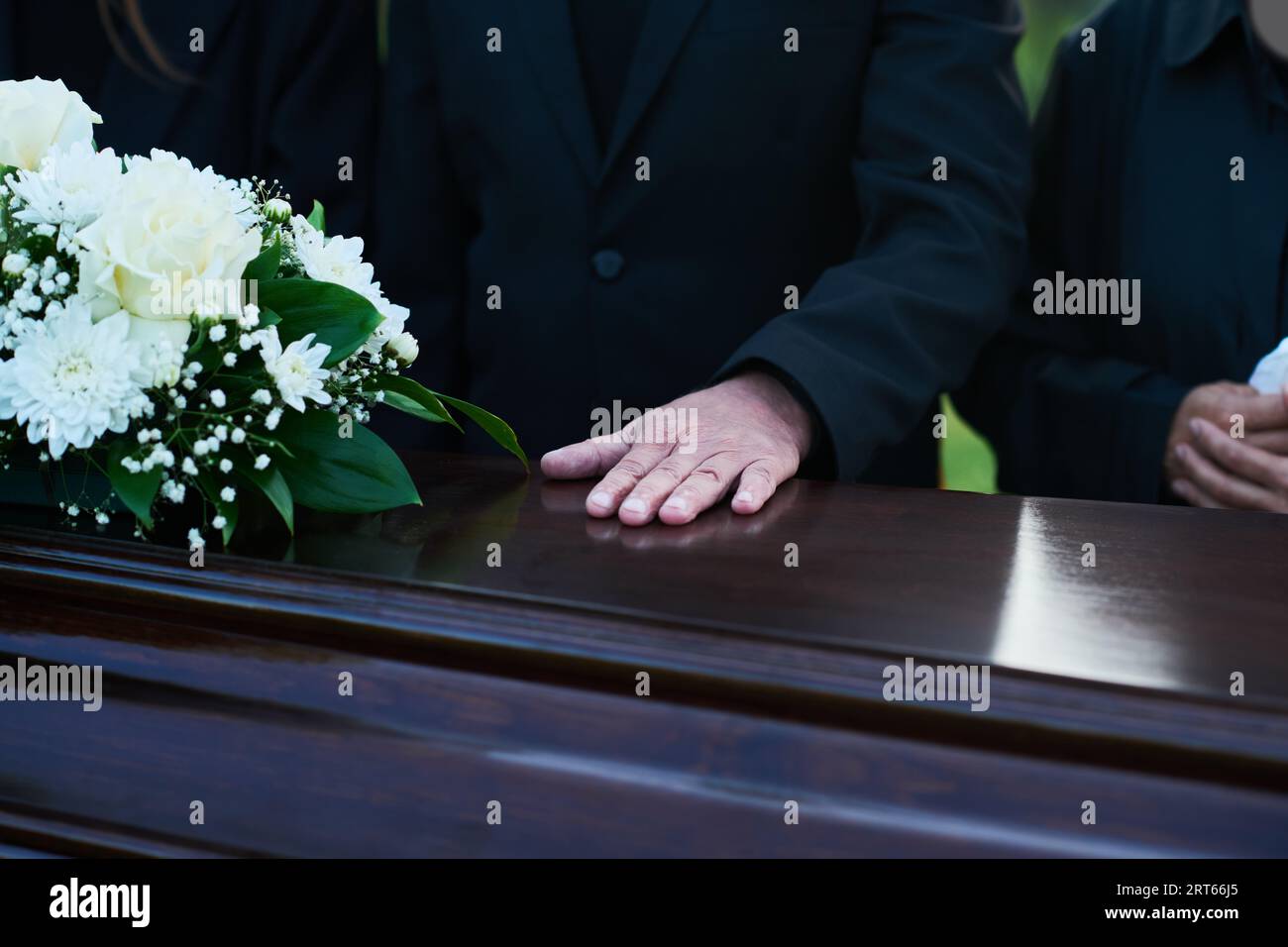 Close-up of mature man keeping hand on top of closed lid of coffin with ...
