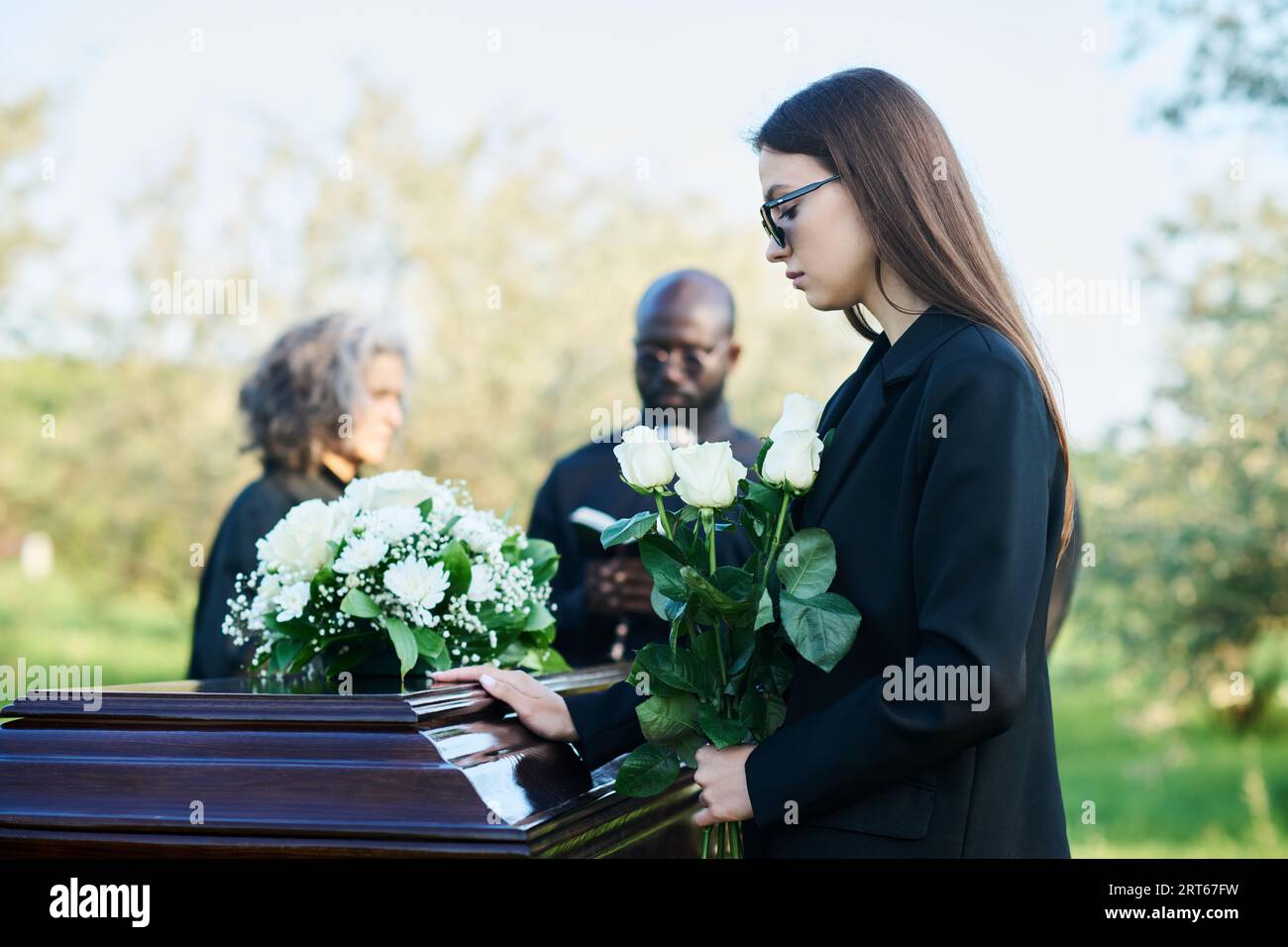 Side view of young mourning woman with bunch of white roses standing by ...