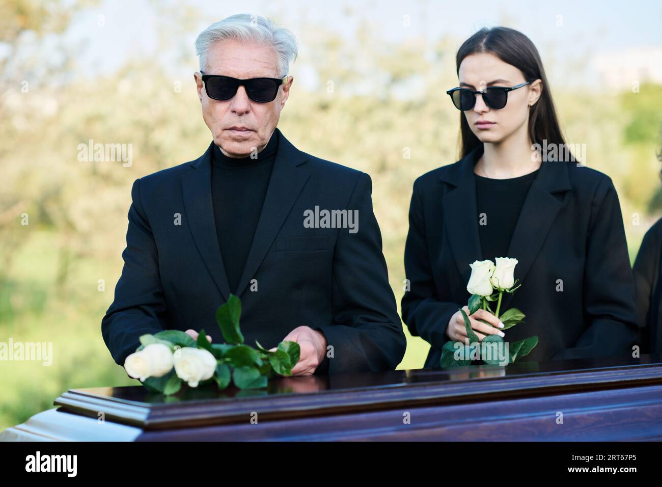 Mature man and his daughter in sunglasses and mourning attire standing ...