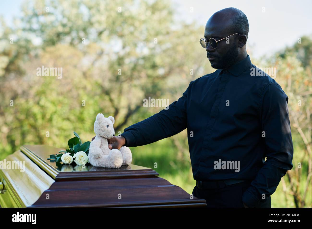 Young grieving African American man in mourning clothes putting bunch ...