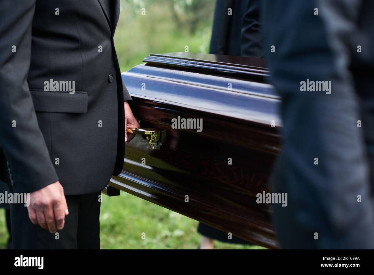 Focus on man in black suit holding by handle of wooden coffin while ...