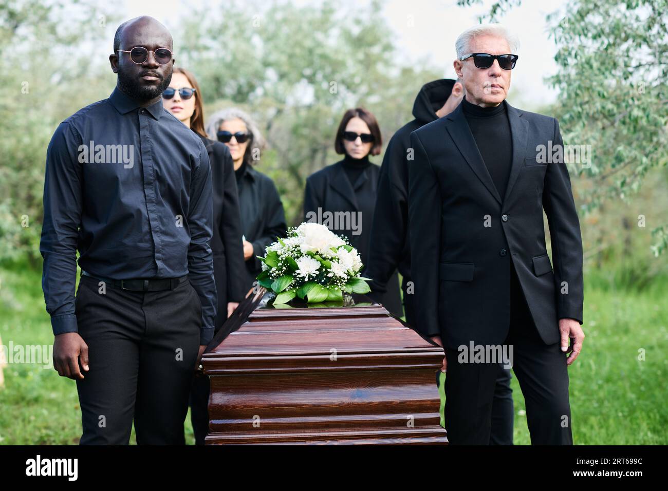 Group of grieving people in mourning attire carrying wooden coffin with ...