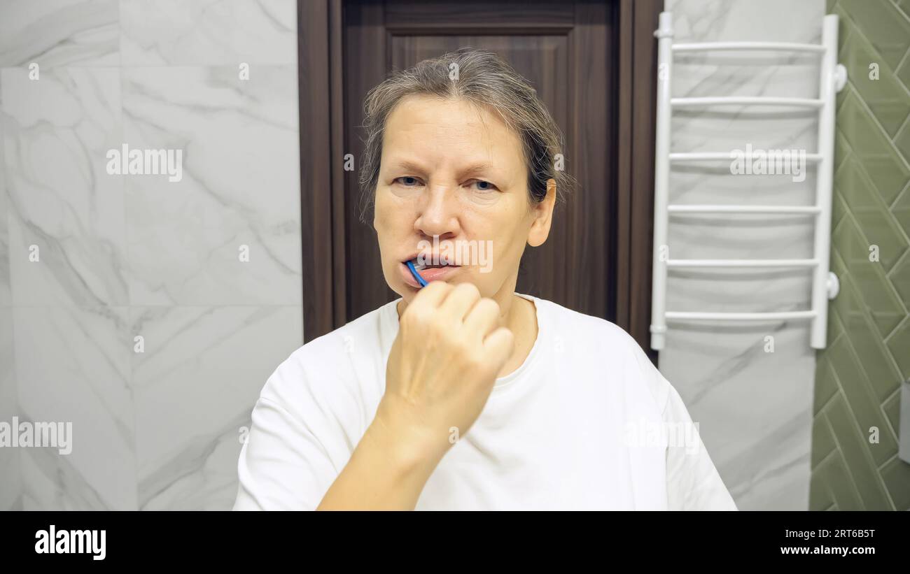 Mature woman brushing teeth with tired expression in bathroom Stock ...