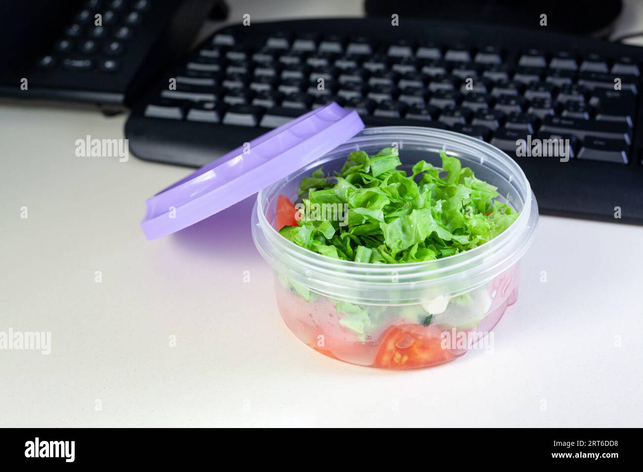 Lunch on work place. Food box container with fresh salad on the working ...