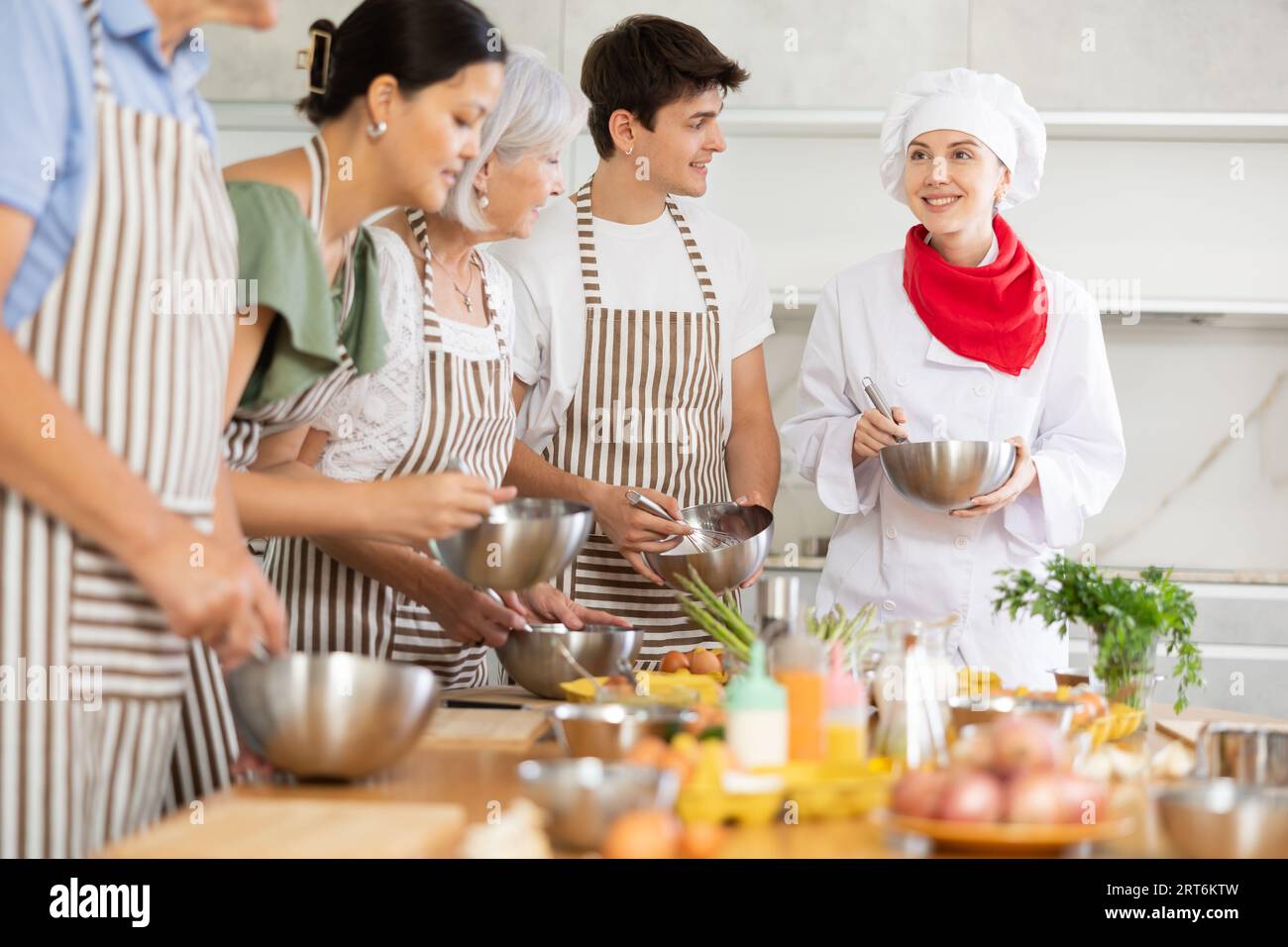Female chef giving instructions to students standing around table in ...