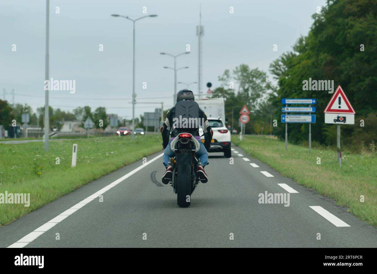 Back rear view of biker driving on asphalt road in a rural area with ...
