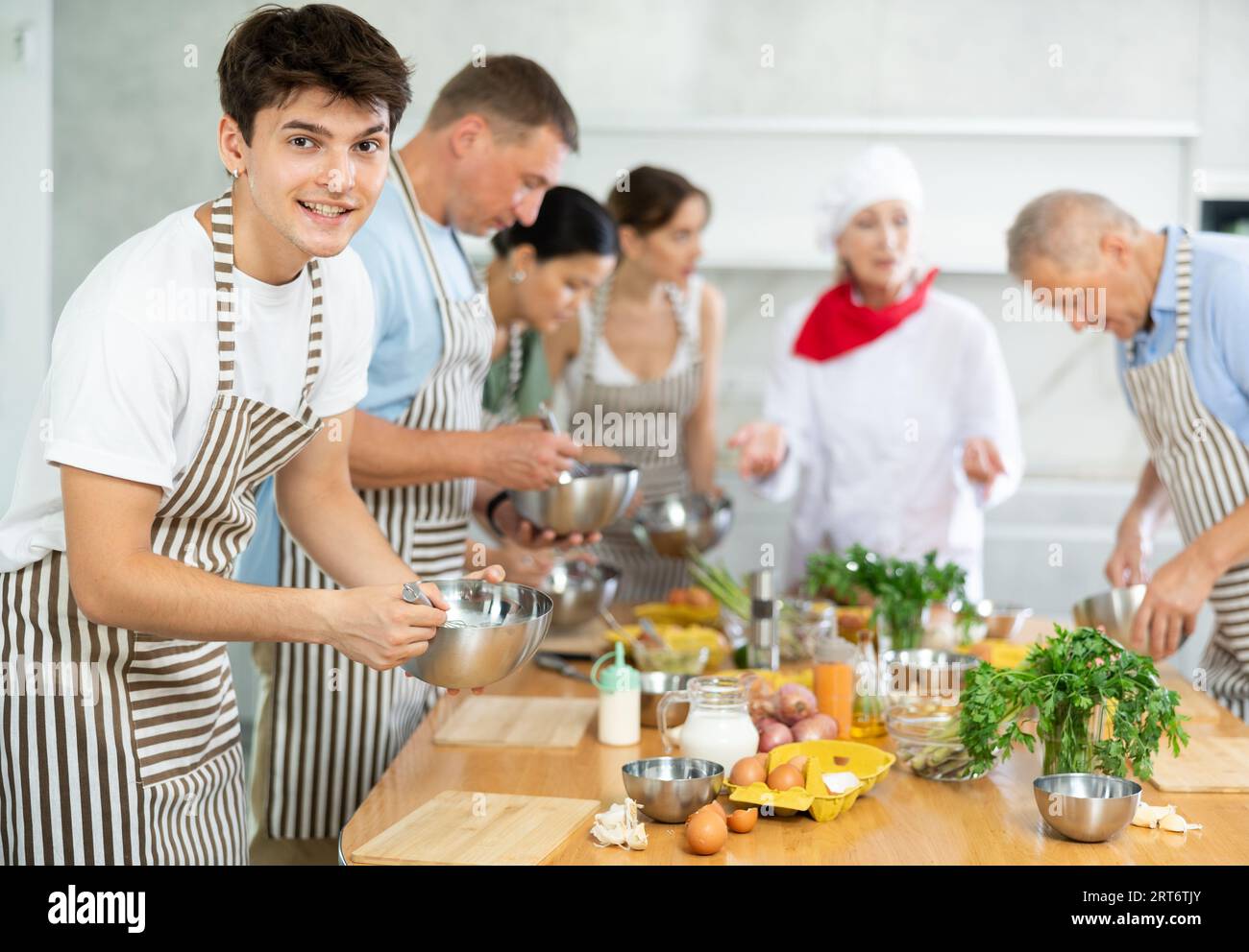 Adult students prepare food according to recipe in cooking class led by ...