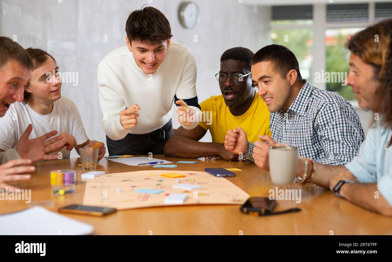 Group of enthusiastic men playing board game sitting around table Stock ...