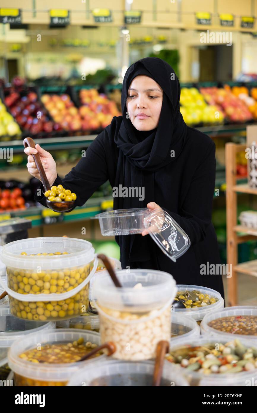 Asian woman in dark blue hijab puts handful of olives in disposable ...