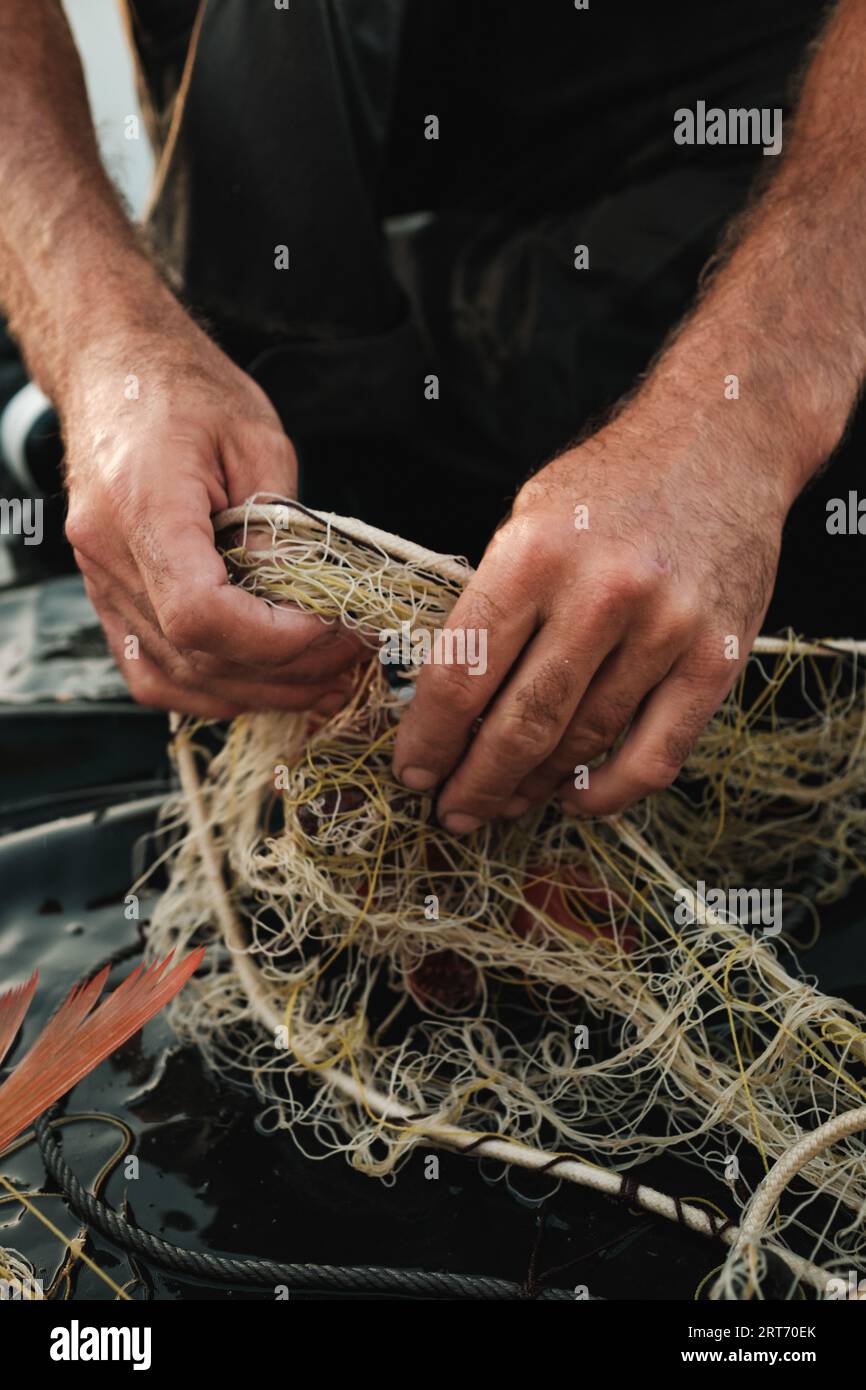 Cropped unrecognizable male untangling fishing net on wet boat deck ...