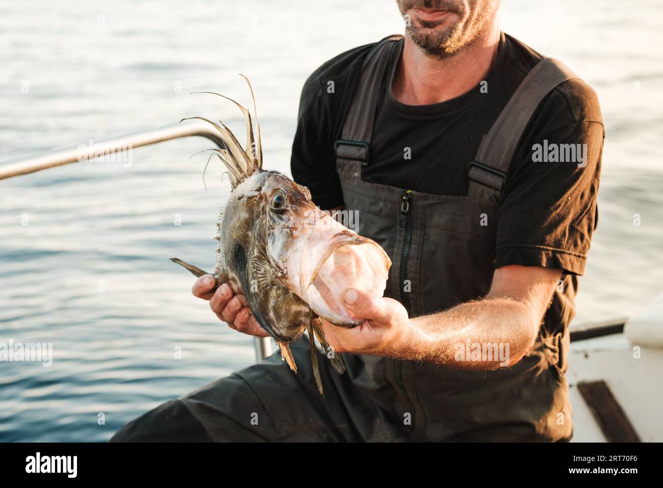 Crop anonymous male in bib and brace overall while sitting on deck of ...