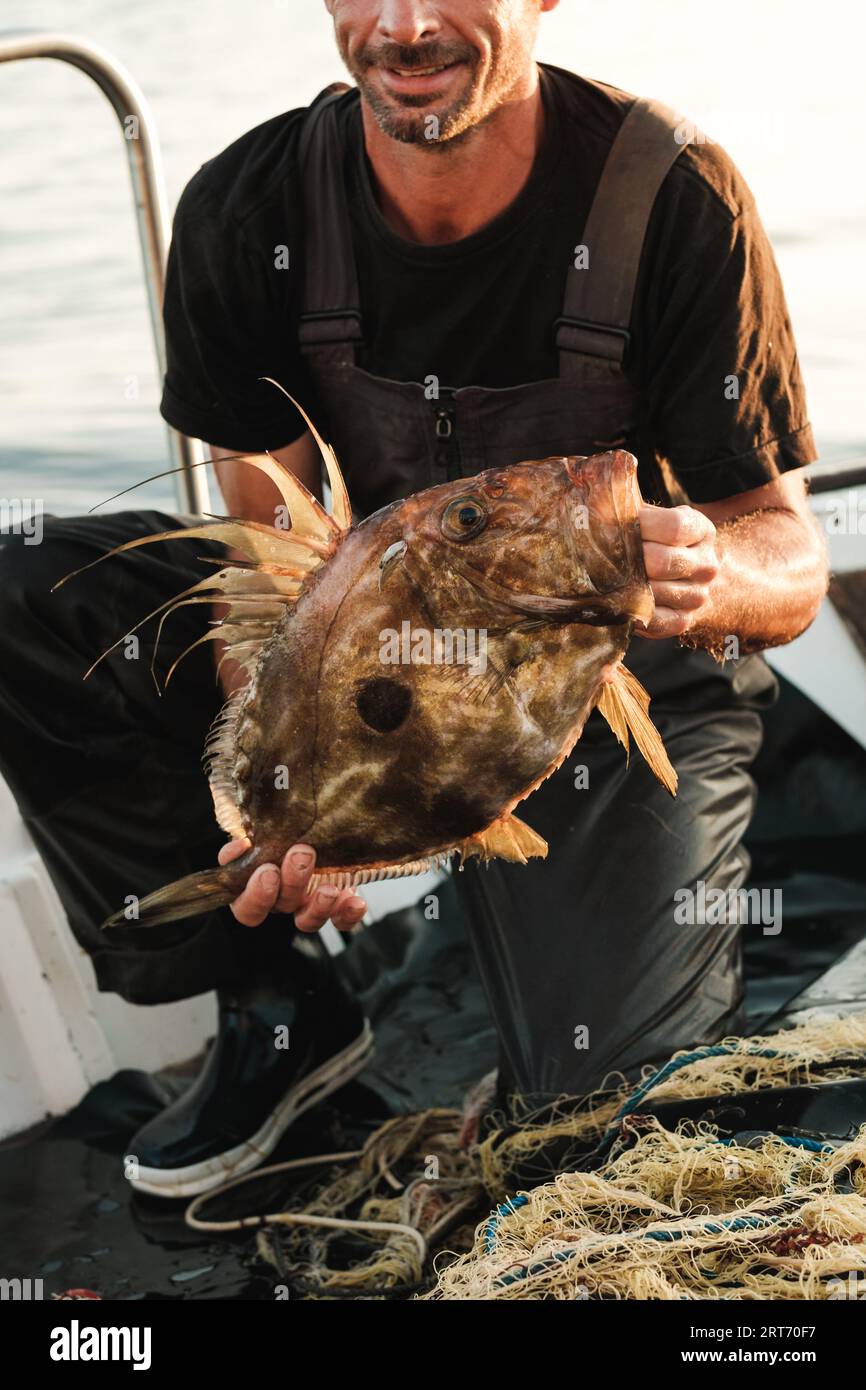 Crop anonymous male in bib and brace overall while sitting on deck of ...
