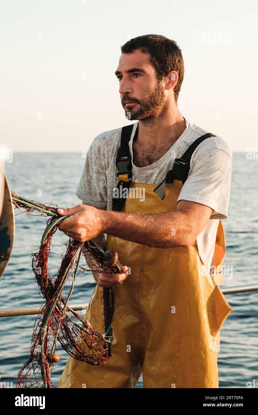 Focused bearded male fisher in uniform seiner hunting fish with net ...
