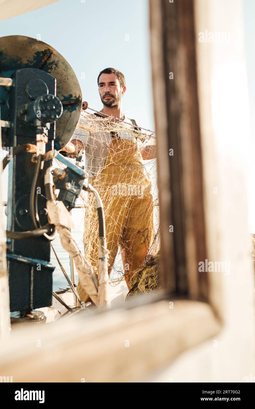 From below focused bearded male fisher in uniform seiner hunting fish ...