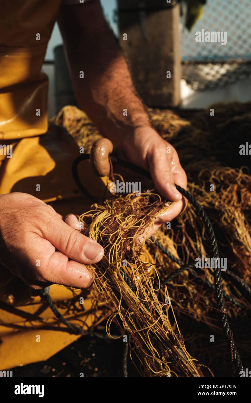 Cropped unrecognizable male untangling fishing net on wet boat deck ...