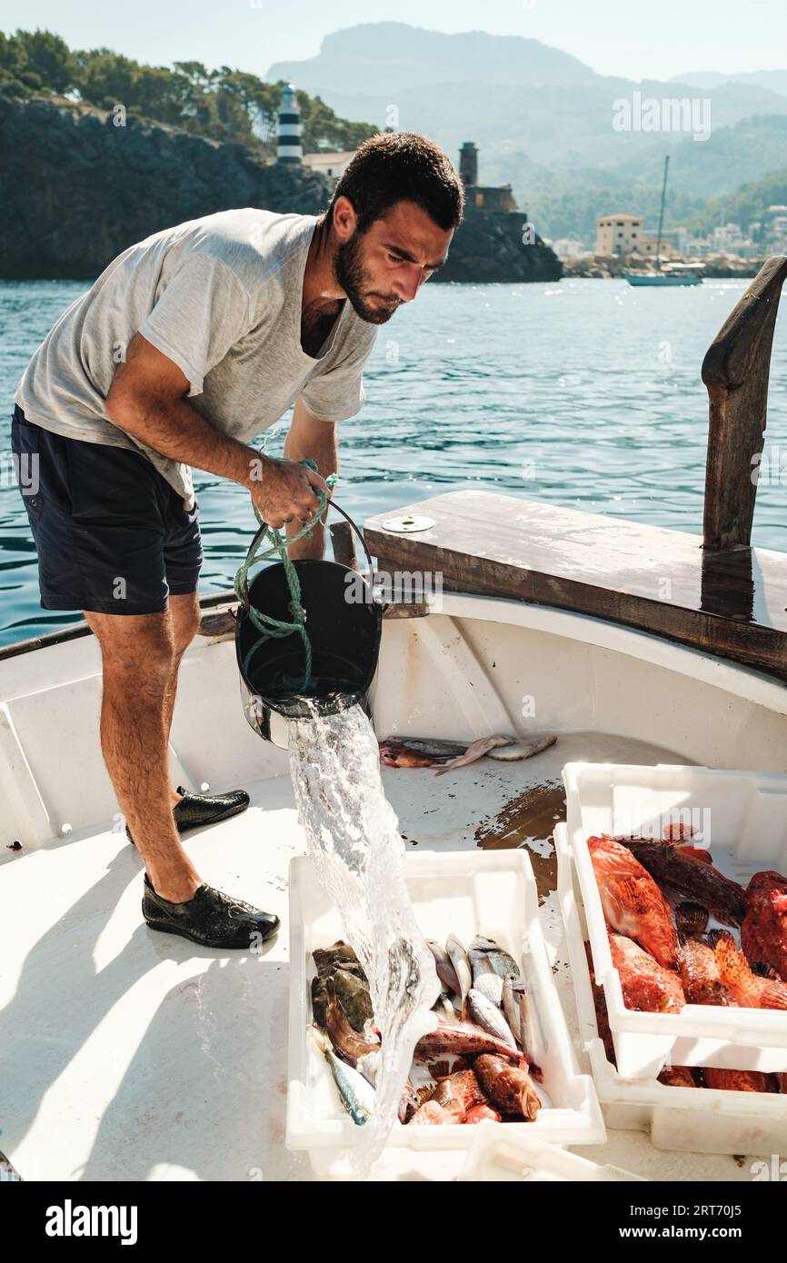 Full body of serious Hispanic male pouring water from bucket on fish in ...