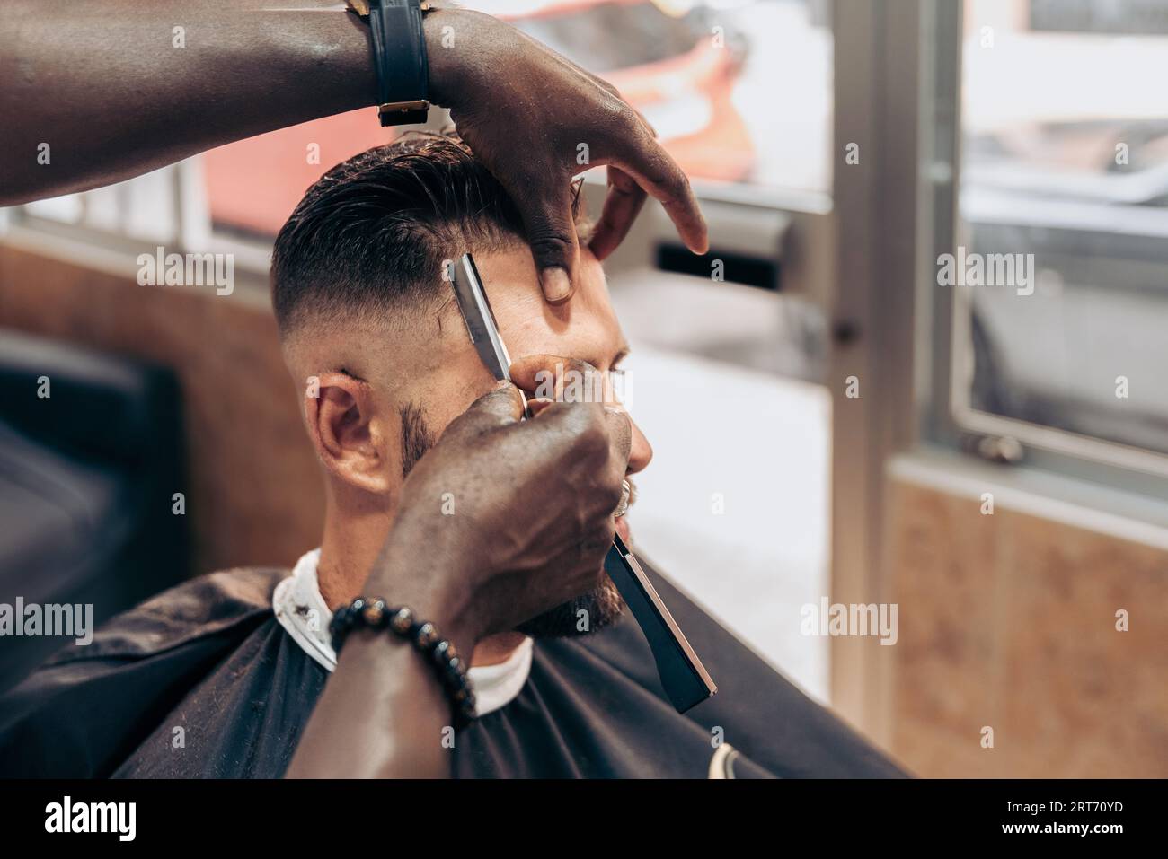 High angle of crop anonymous African American barber using razor while ...