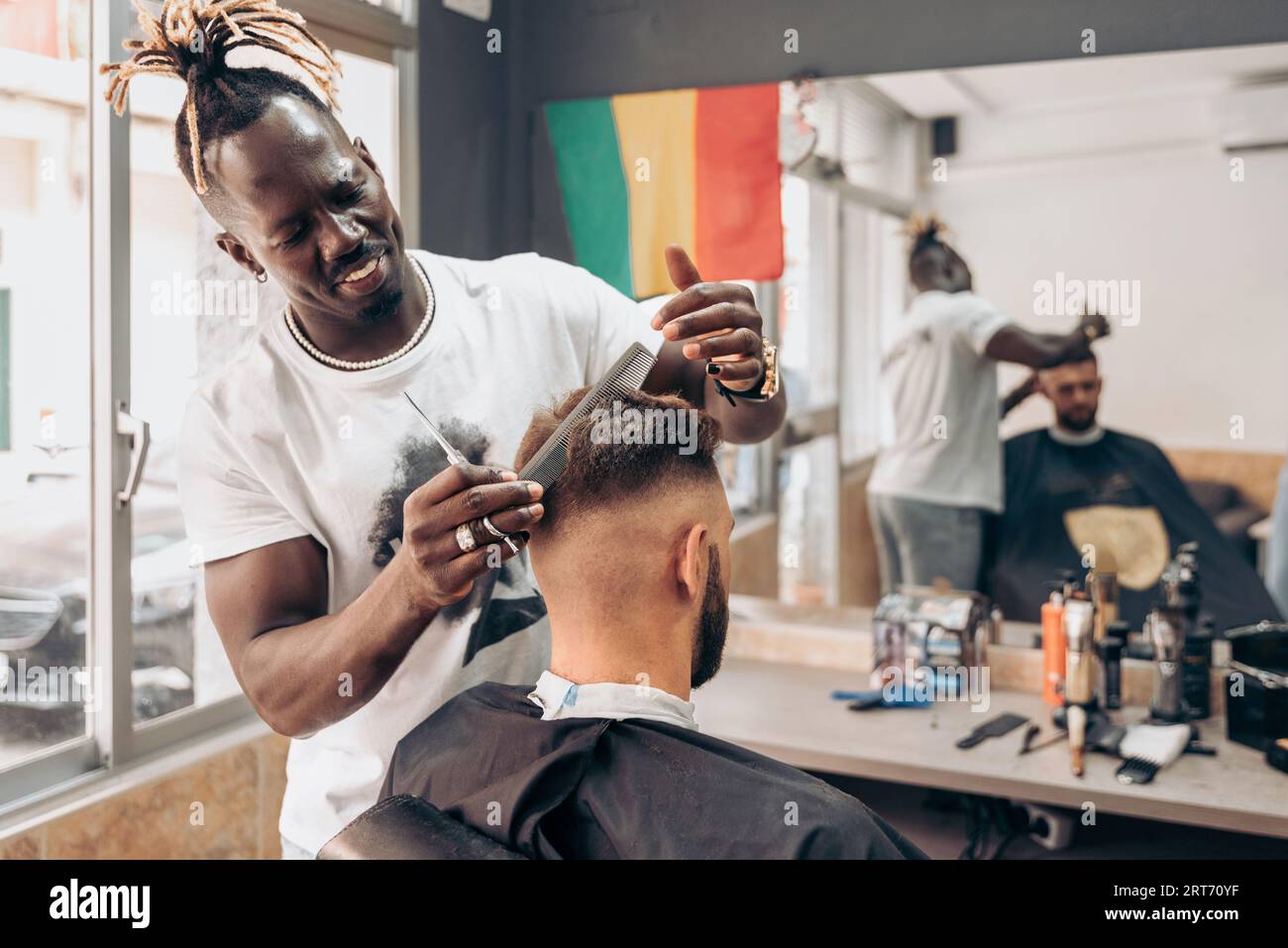 Positive African American barber using comb and scissors while cutting ...