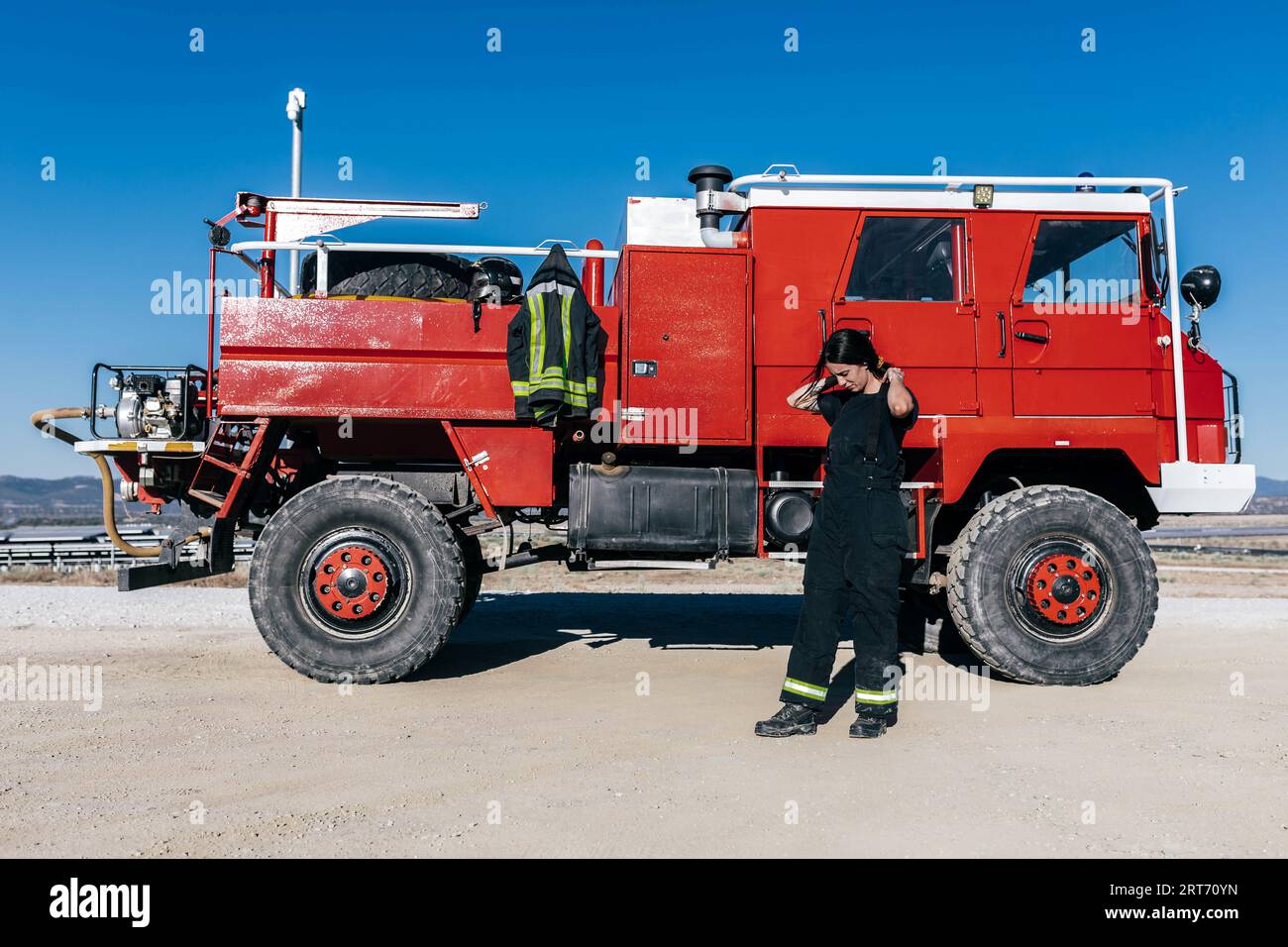Full body of female firefighter wearing workwear adjusting hair while ...
