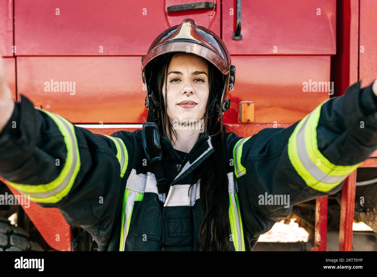 Young female firefighter in uniform standing against red fire truck and ...