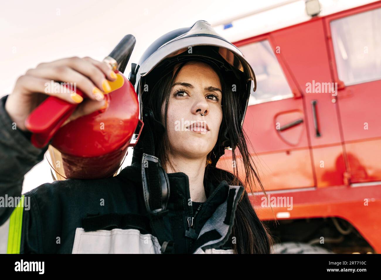 Low angle of young female firefighter wearing protective uniform and ...