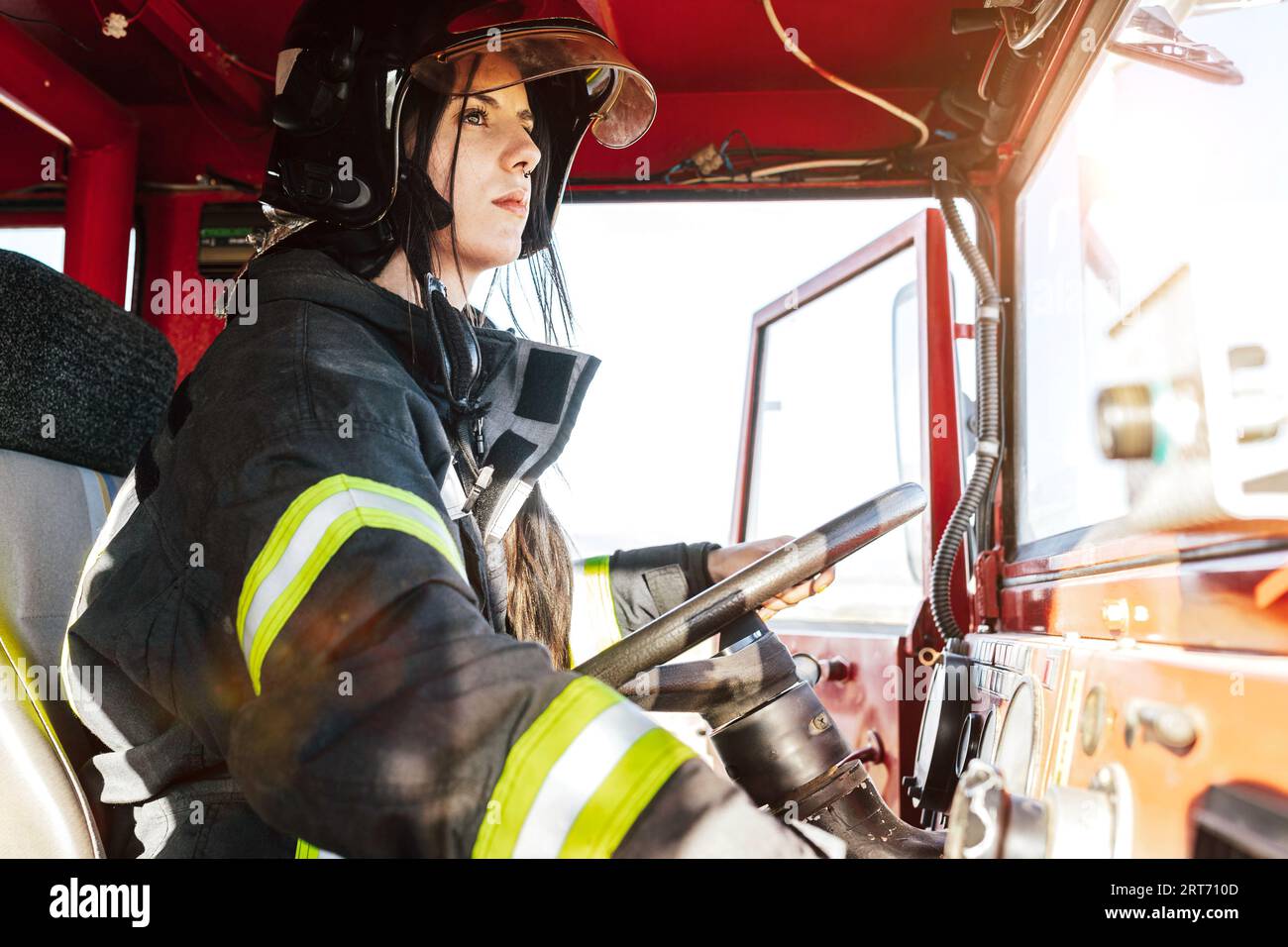 Young female firefighter in protective uniform and helmet driving red ...