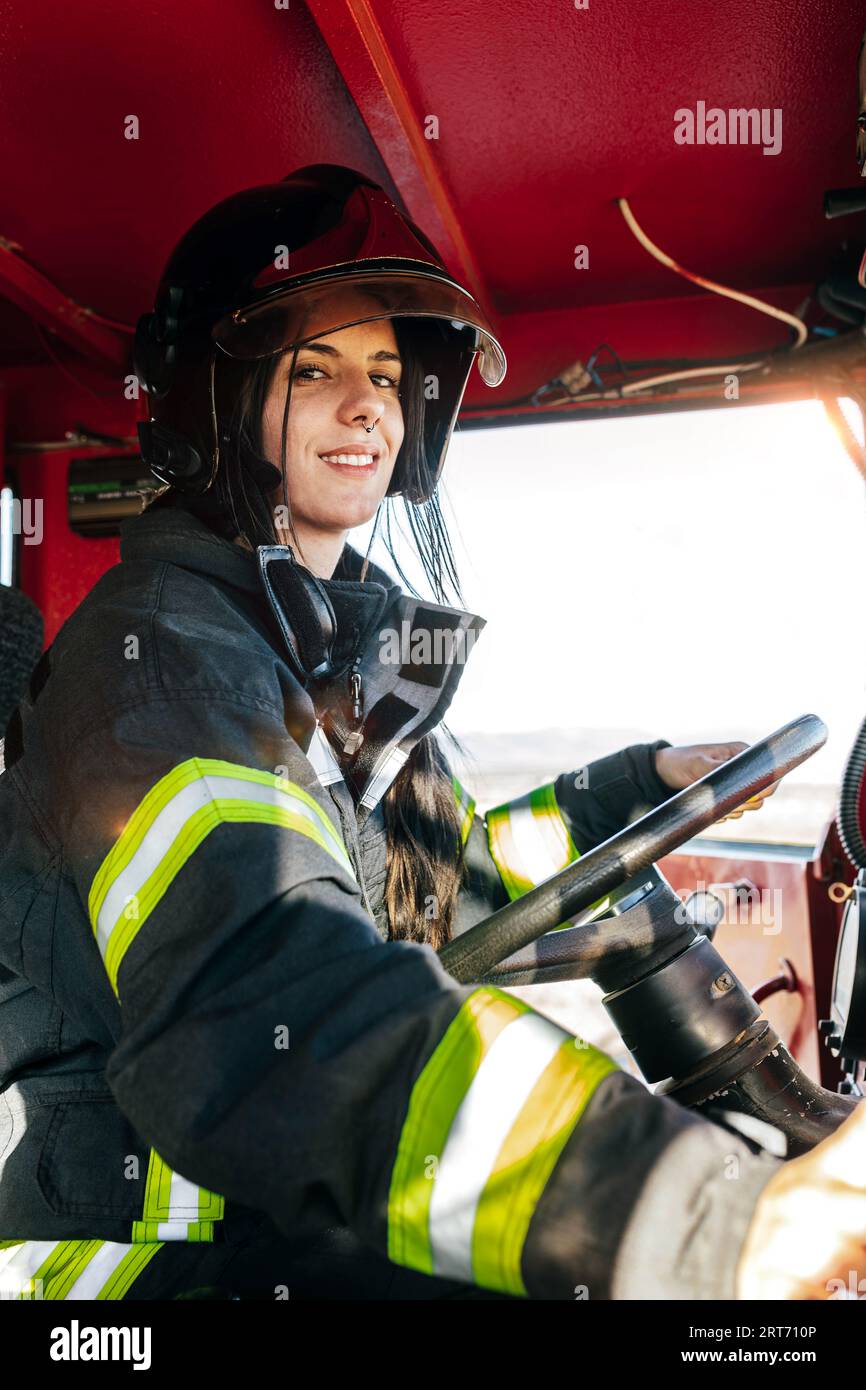 Young positive female firefighter in protective uniform and helmet ...