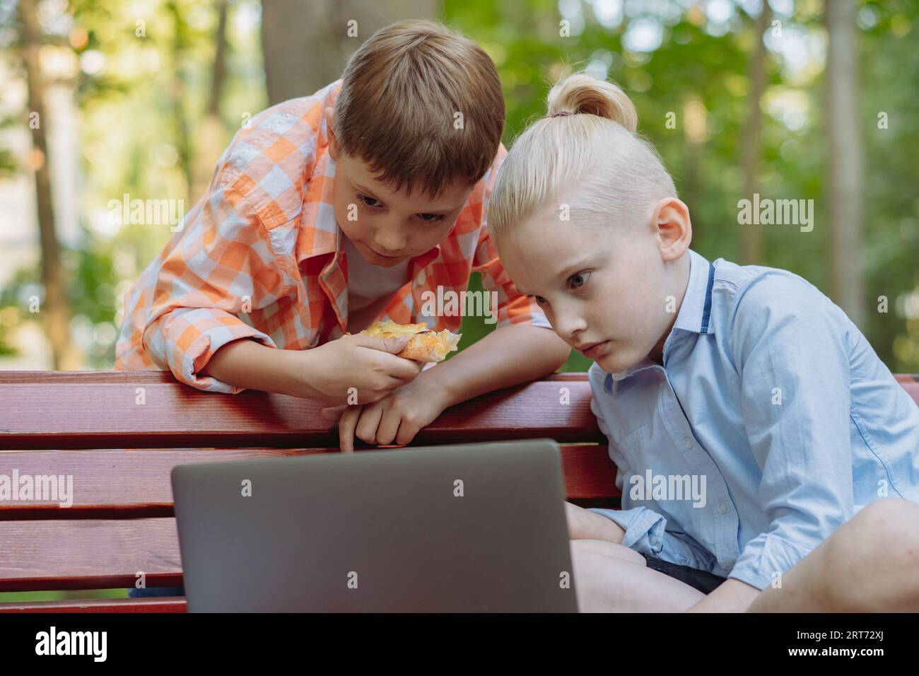 cute caucasian boys sitting on bench in park with laptop computer. Black screen Stock Photo - Alamy