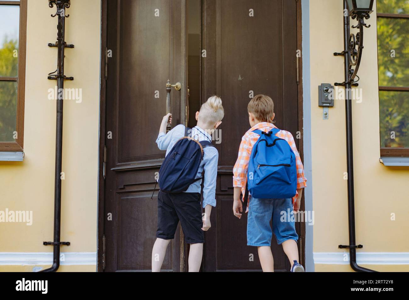 children entering school opening big wooden door. Boys with backpacks ...