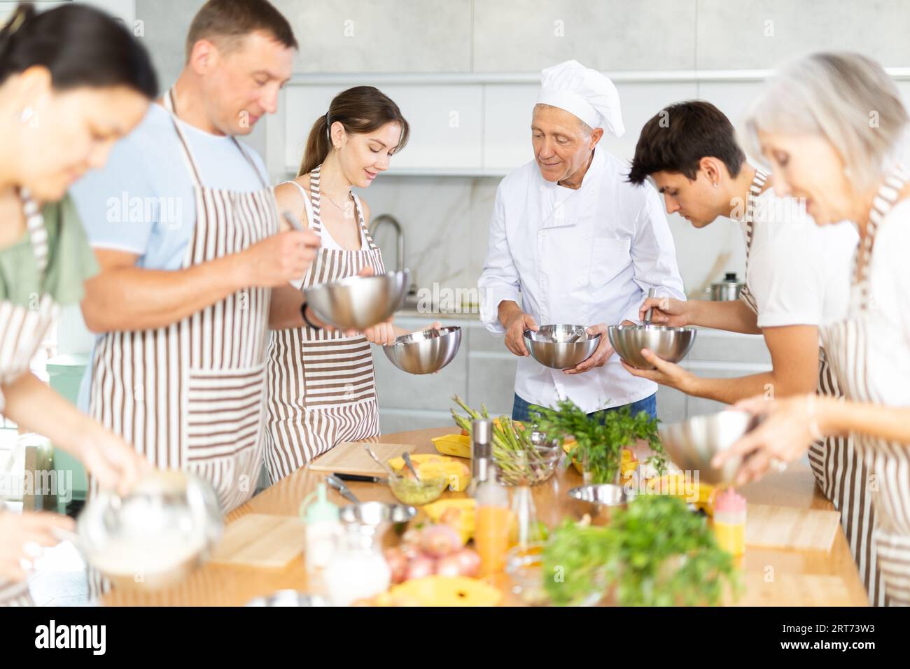 Smiling old man chef of cooking course teaching attendees how to mix ...