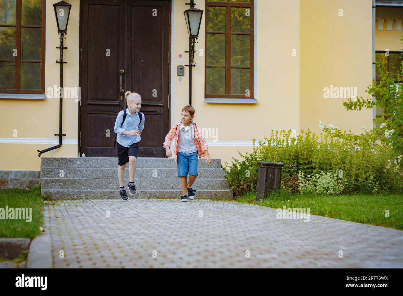 Happy caucasian children running from school with backpacks on sunny ...