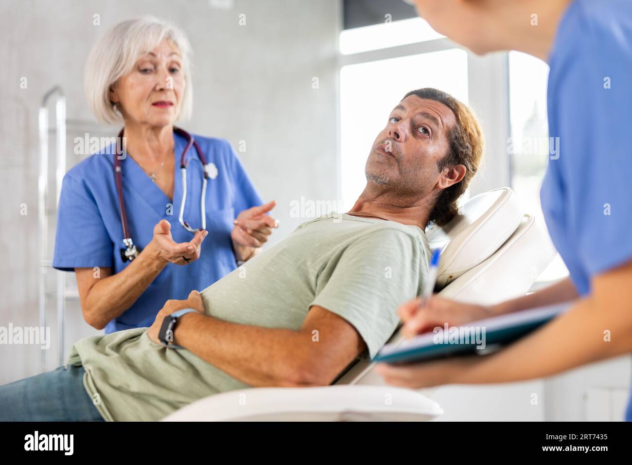 Elderly woman doctor conducting questionnaire of male patient in clinic ...