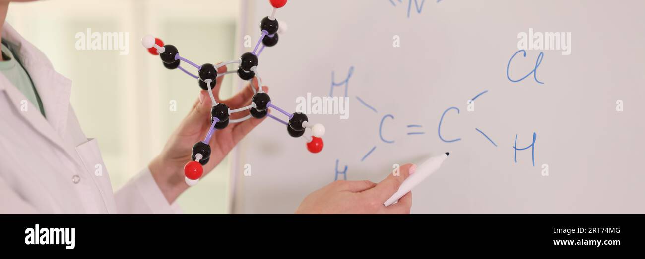 Female chemist holding molecular model and drawing chemical formulas on ...